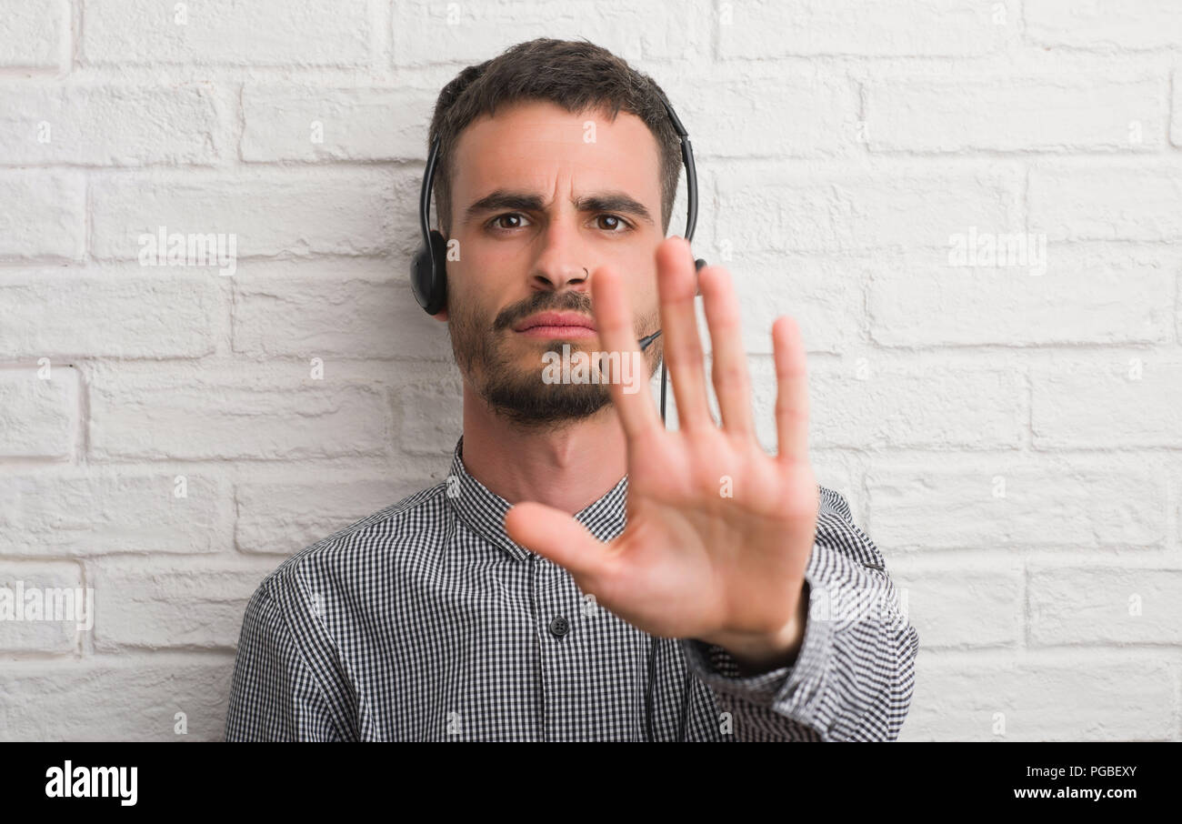 Young adult man over brick wall working as operator with open hand ...