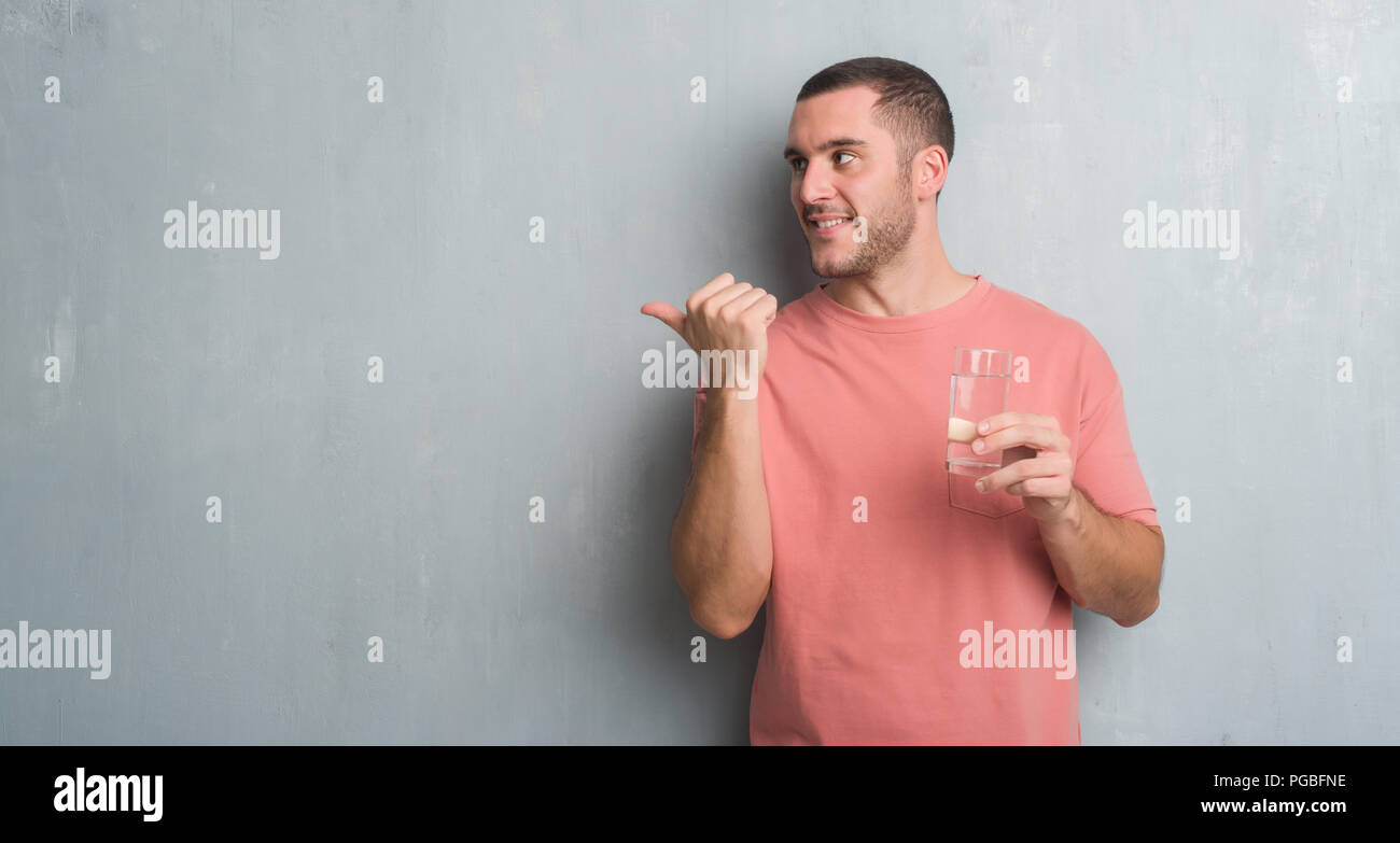Young caucasian man over grey grunge wall drinking a glass of water ...