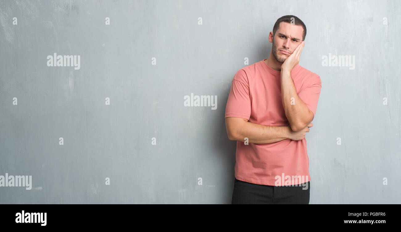 Young caucasian man over grey grunge wall thinking looking tired and ...