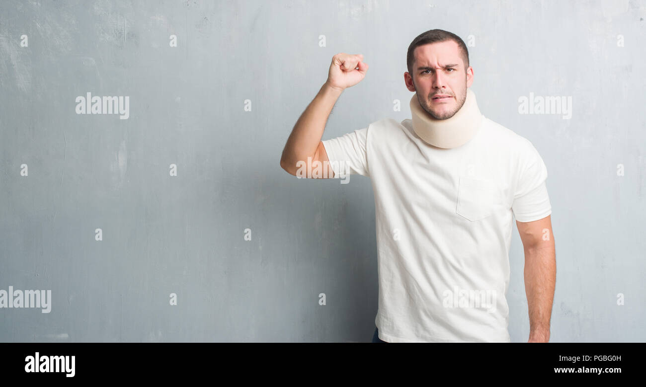 Young caucasian man injured over grey grunge wall wearing neck collar ...