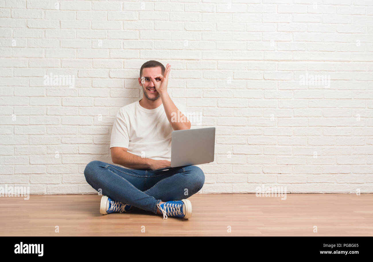 Young caucasian man sitting over white brick wall using computer laptop ...