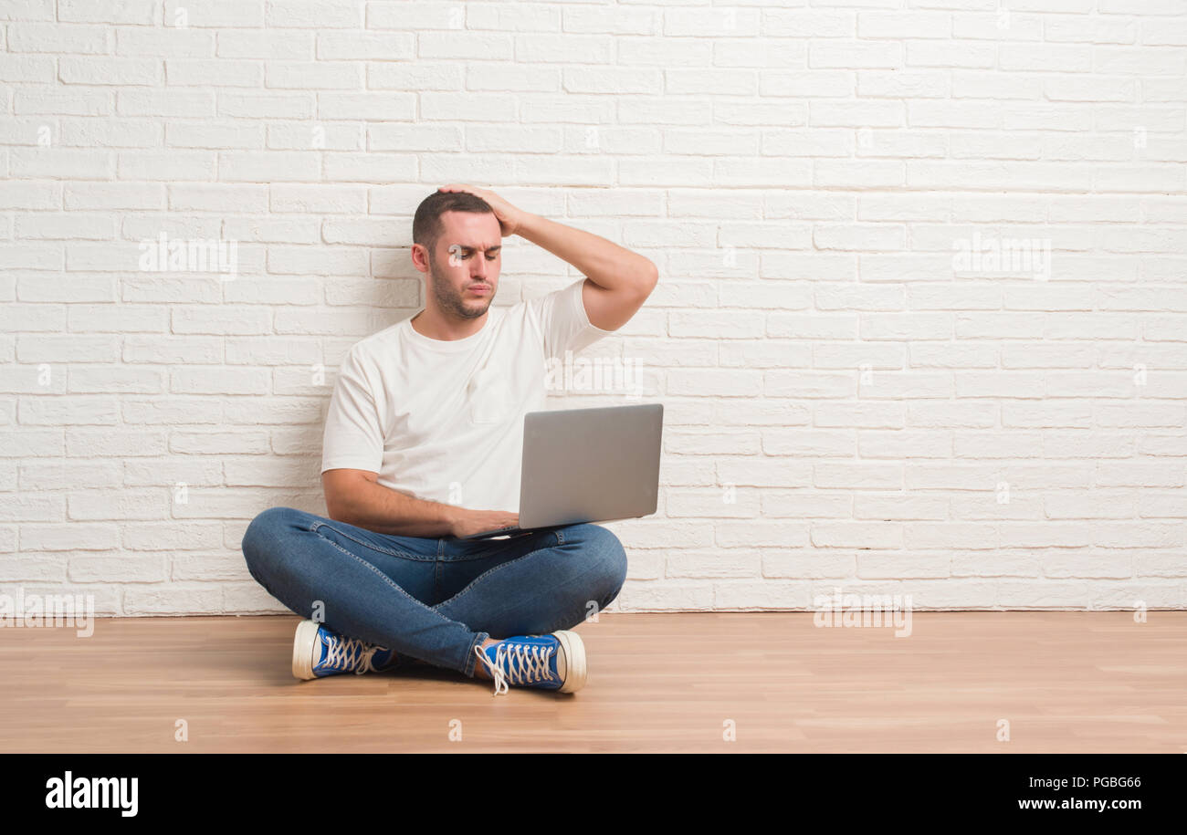 Young caucasian man sitting over white brick wall using computer laptop ...