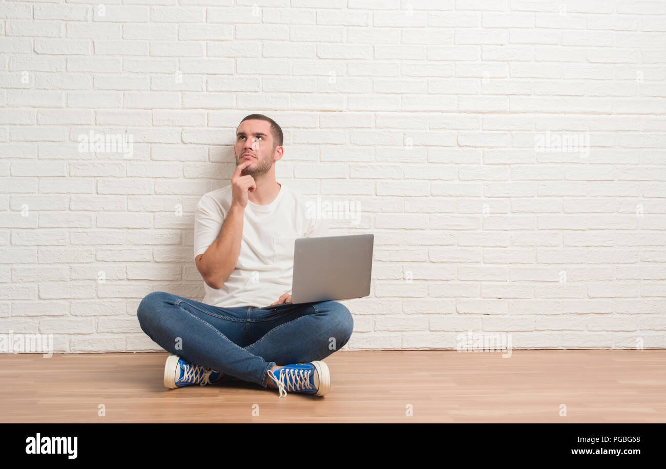 Young caucasian man sitting over white brick wall using computer laptop ...