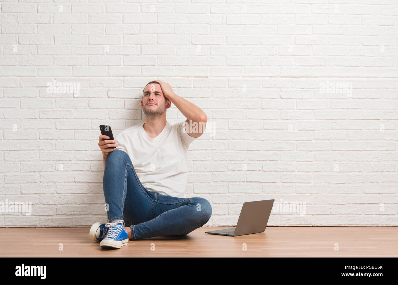 Young caucasian man sitting over white brick wall using computer laptop ...