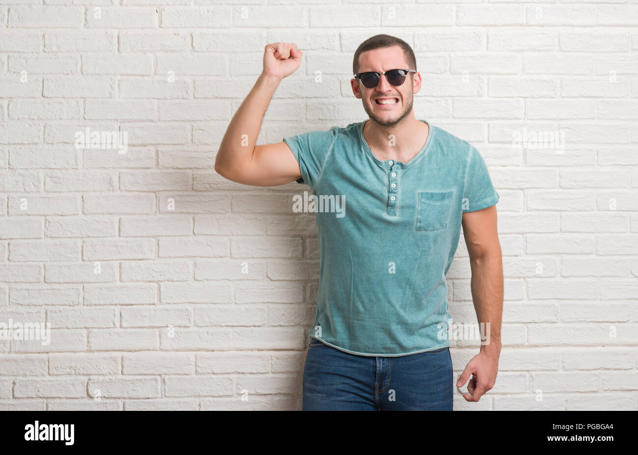 Young caucasian man standing over white brick wall wearing sunglasses ...