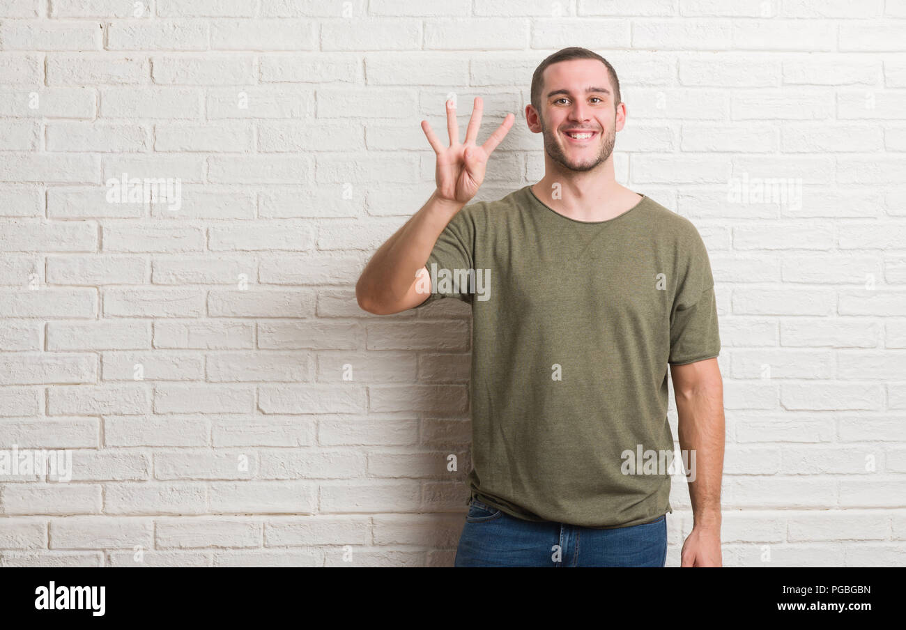 Young caucasian man standing over white brick wall showing and pointing ...