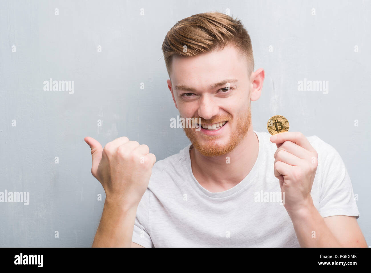 Young redhead man over grey grunge wall showing bitcoin pointing and ...