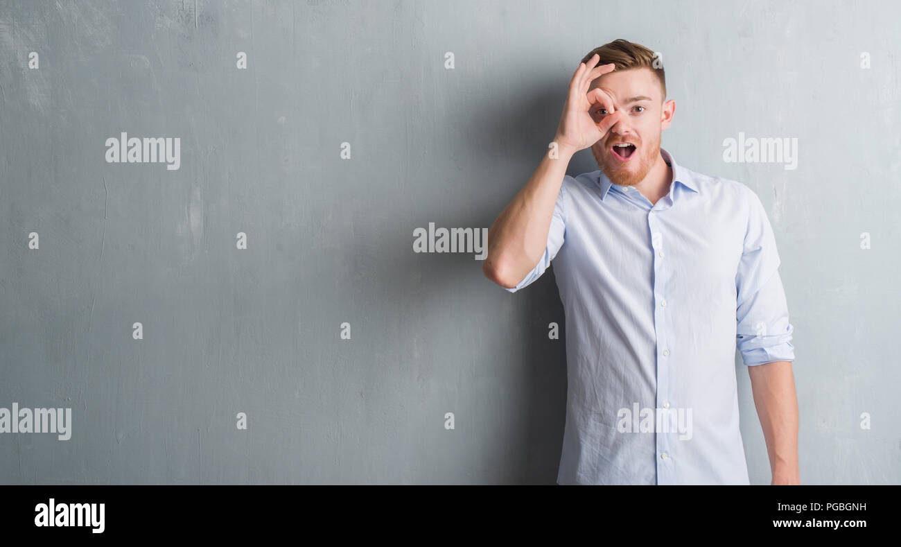 Young redhead business man over grey grunge wall doing ok gesture ...