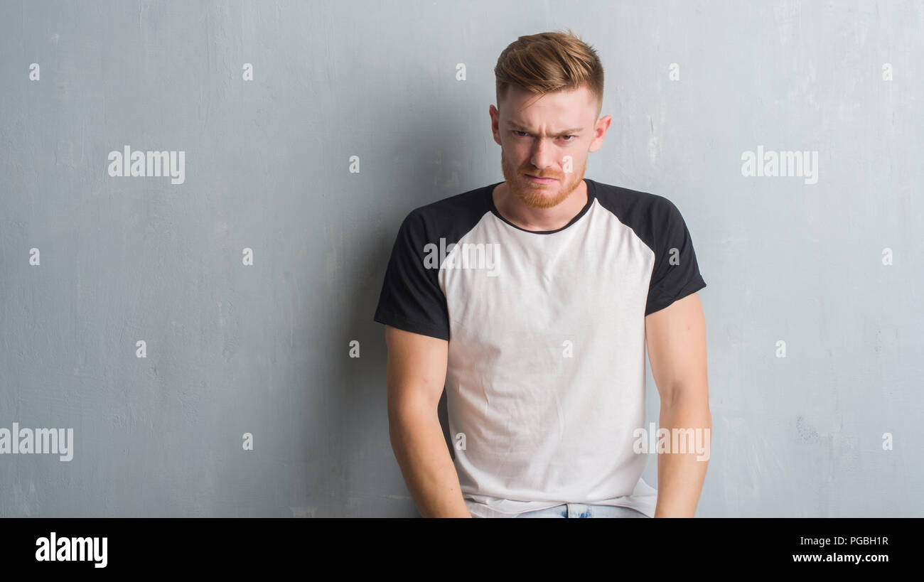 Young redhead man over grey grunge wall depressed and worry for ...