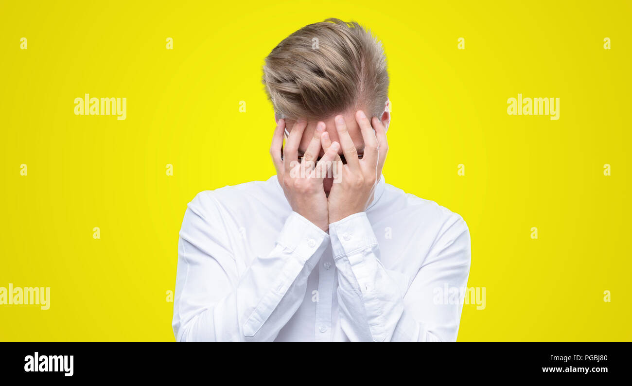Young handsome blond man with sad expression covering face with hands ...