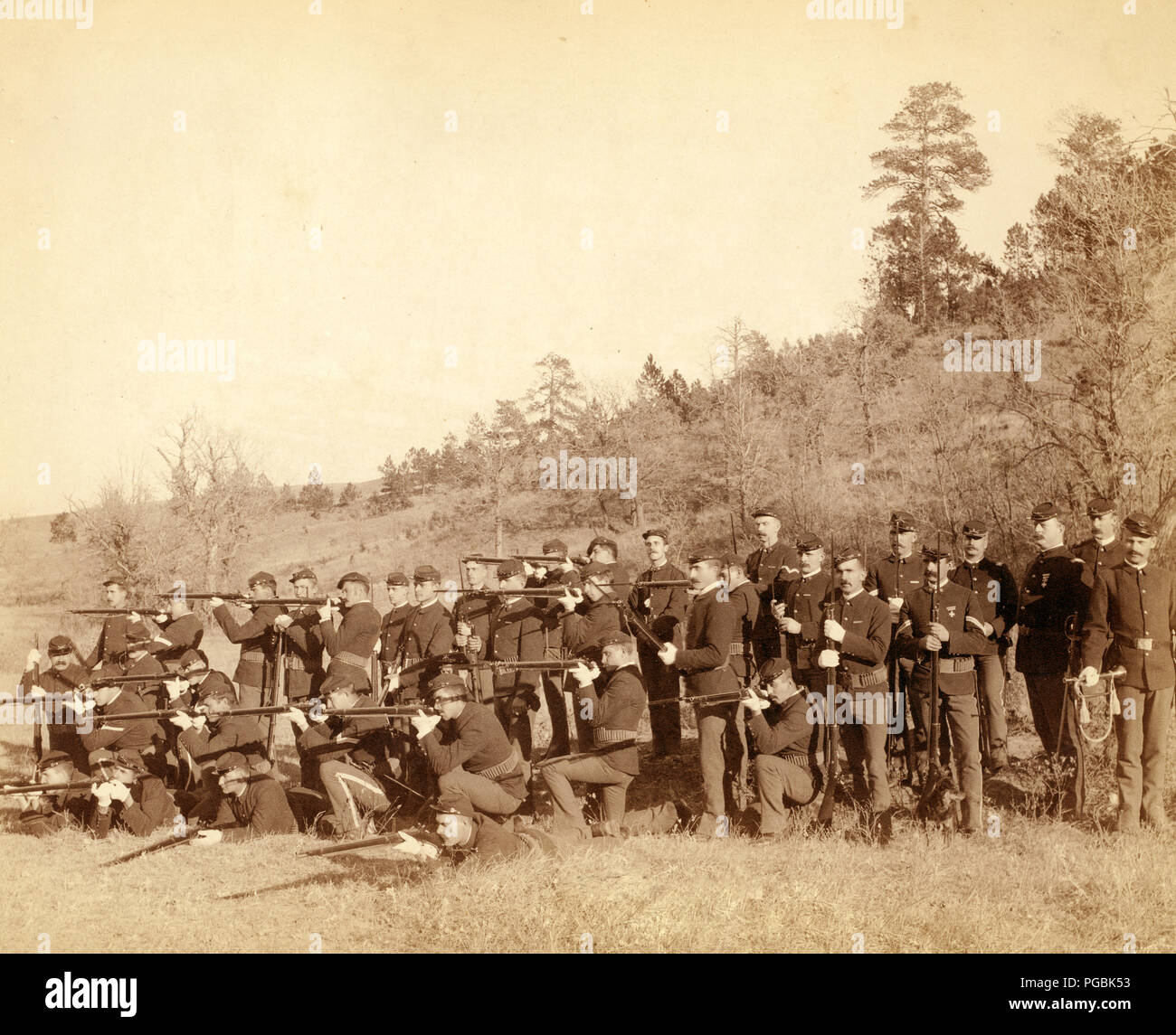 Group of uniformed military men with rifles next to a hillside; part of ...