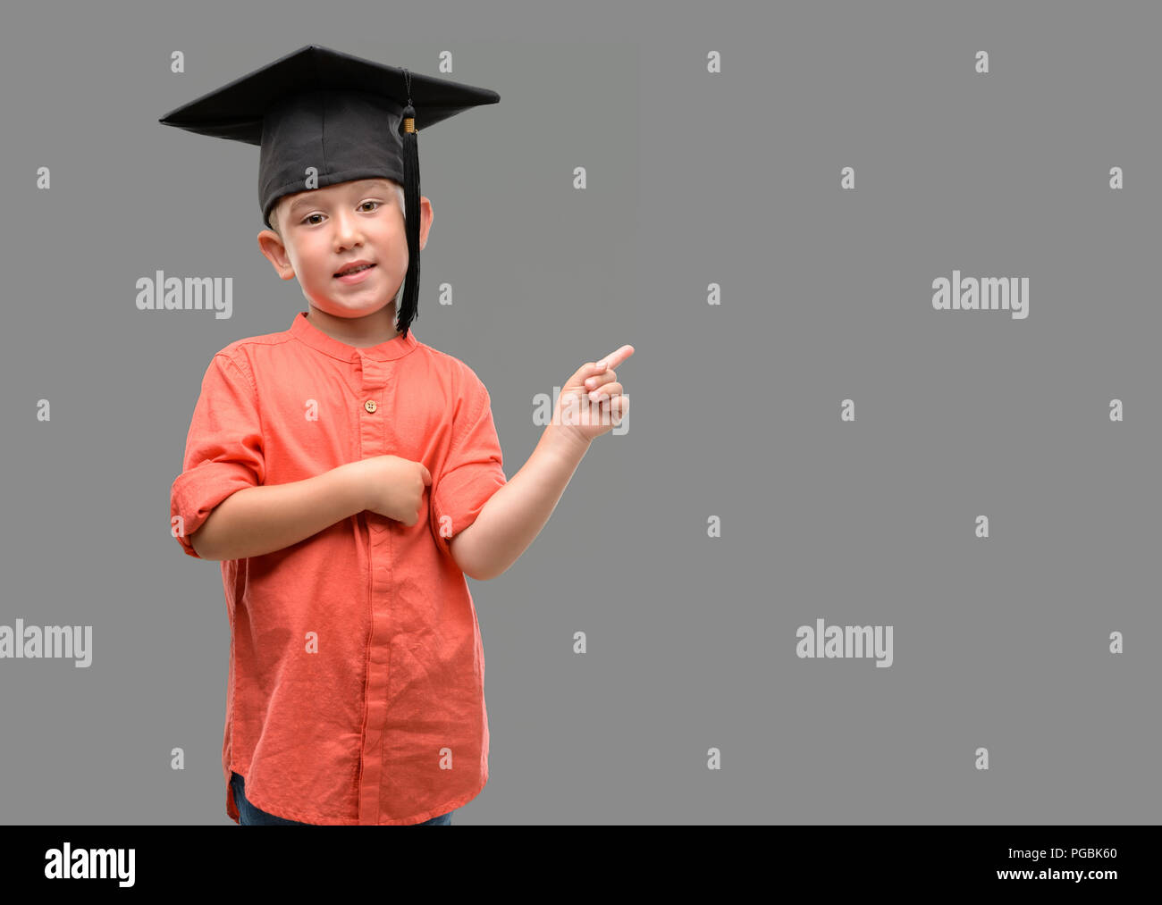 Dark haired little child wearing graduation cap very happy pointing ...