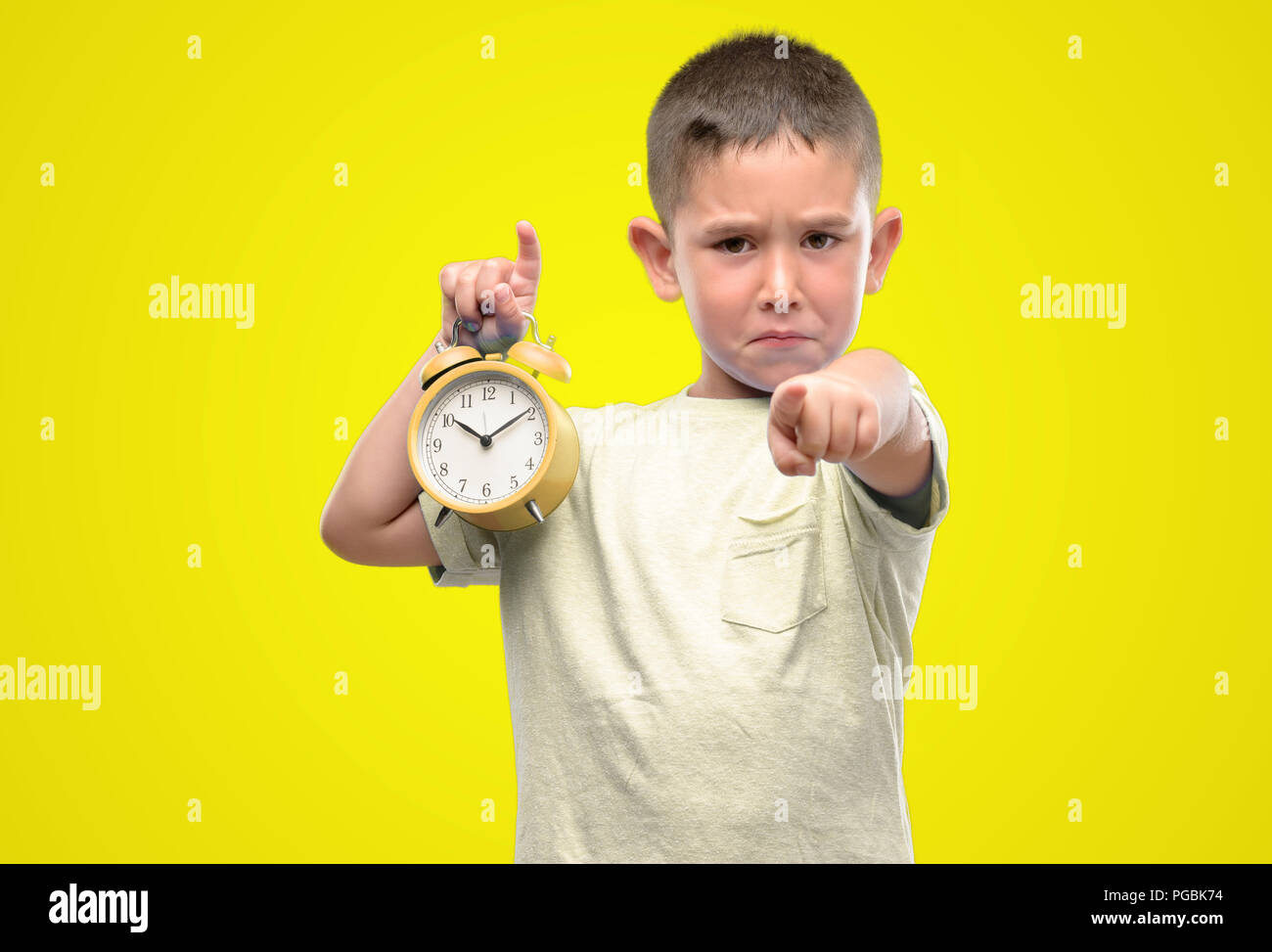 Little child holding alarm clock pointing with finger to the camera and ...