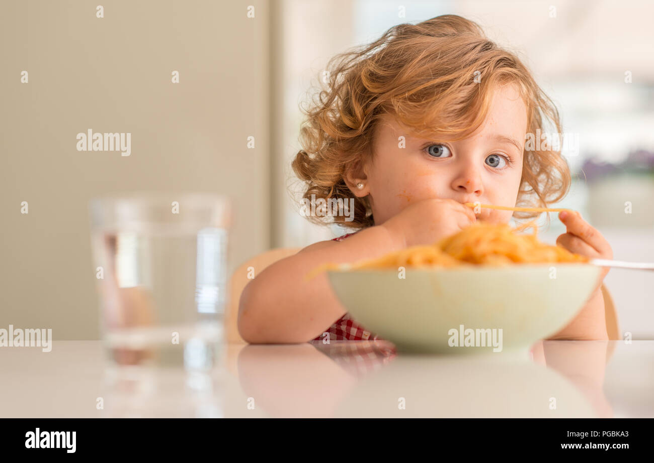 Beautiful blond child eating spaghetti with hands at home Stock Photo ...