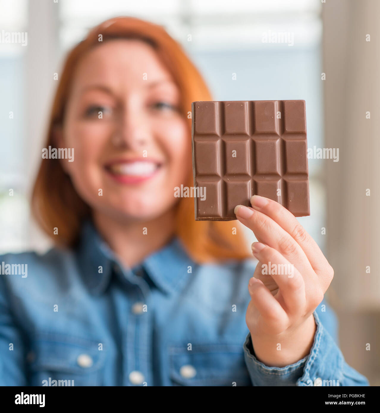 Redhead woman holding chocolate bar at home screaming proud and ...