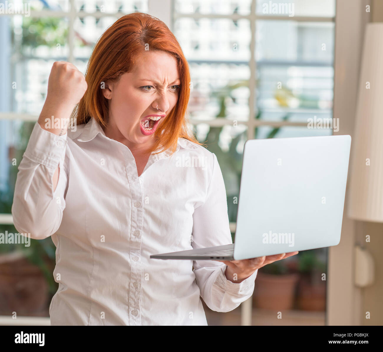 Redhead woman using computer laptop at home annoyed and frustrated ...