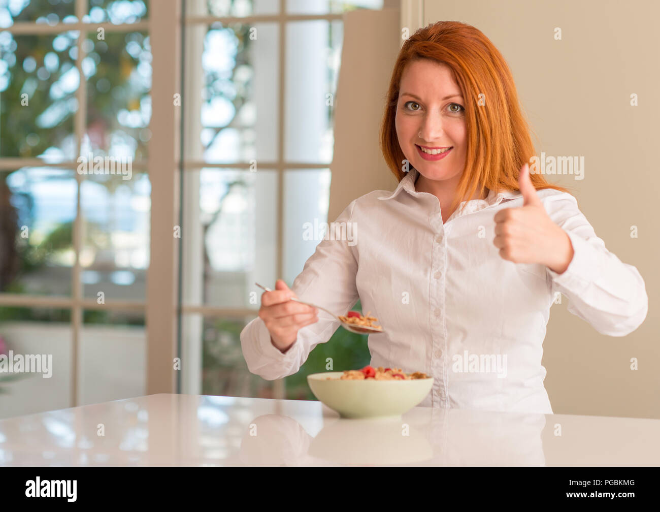 Redhead woman eating cereals with raspberries at home happy with big ...