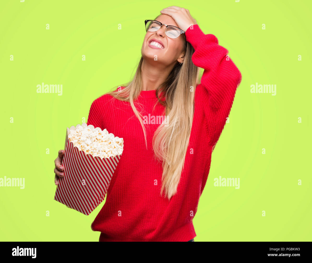 Beautiful young woman eating popcorn stressed with hand on head ...