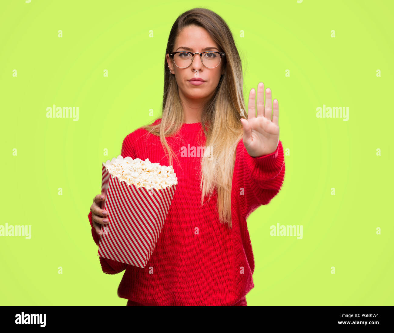 Beautiful young woman eating popcorn with open hand doing stop sign ...