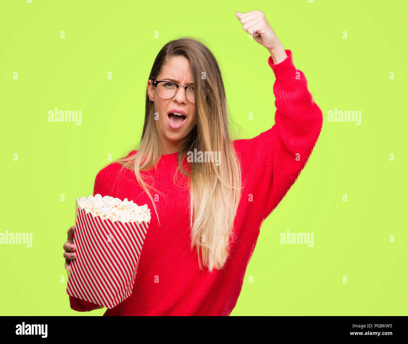 Beautiful young woman eating popcorn annoyed and frustrated shouting ...