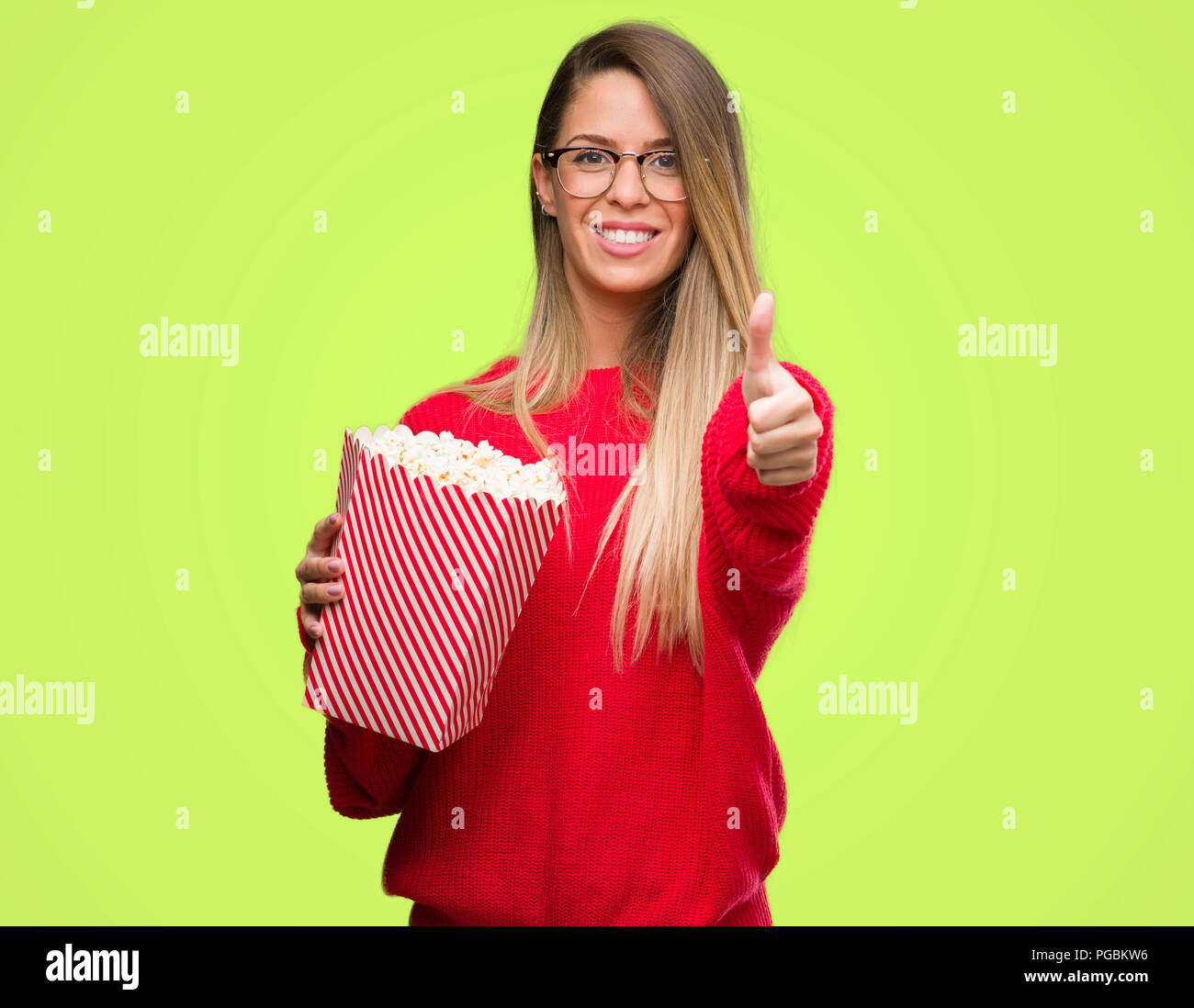 Beautiful young woman eating popcorn happy with big smile doing ok sign ...