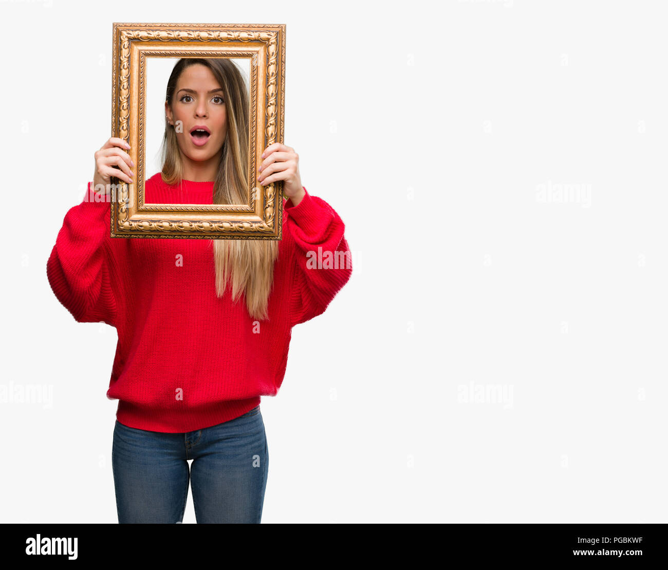 Beautiful young woman holding vintage frame scared in shock with a ...