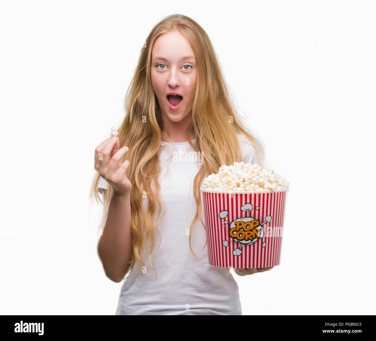 Blonde teenager woman eating pop corn scared in shock with a surprise ...