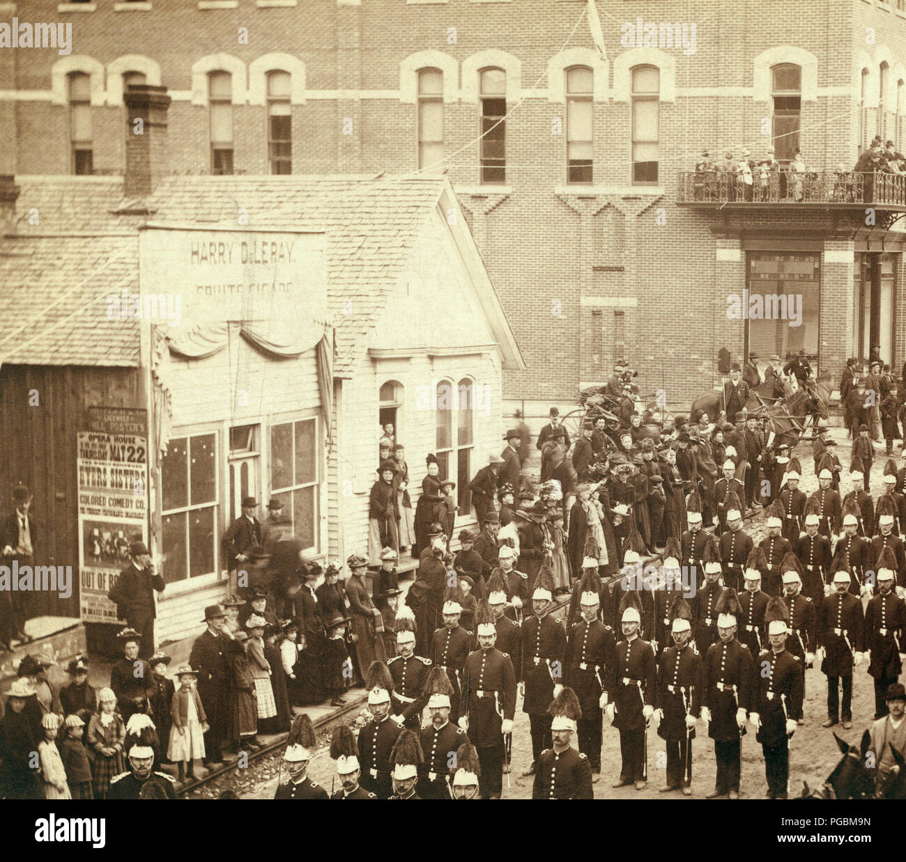 Group of uniformed men standing in street parade; bystanders on side ...