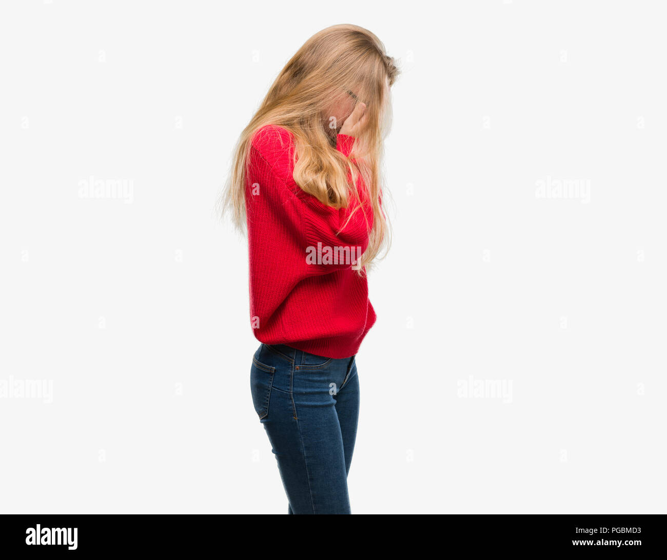 Blonde teenager woman wearing red sweater with sad expression covering ...