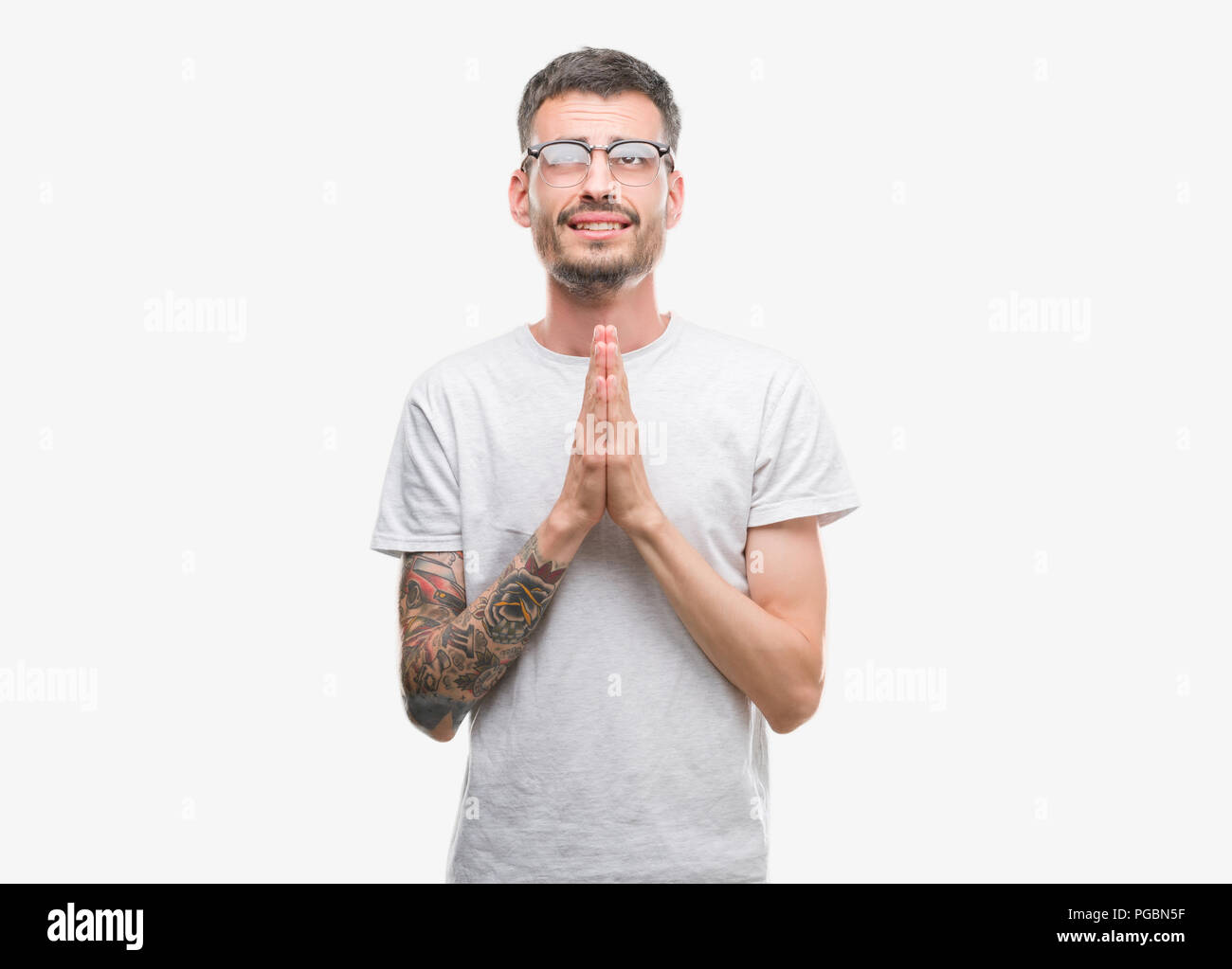 Young tattooed adult man begging and praying with hands together with ...