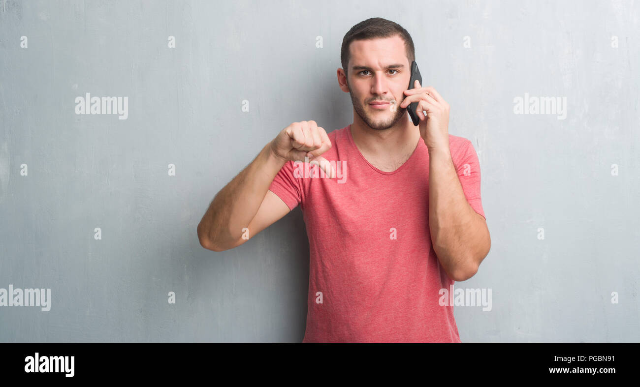 Young caucasian man over grey grunge wall talking on the phone with ...