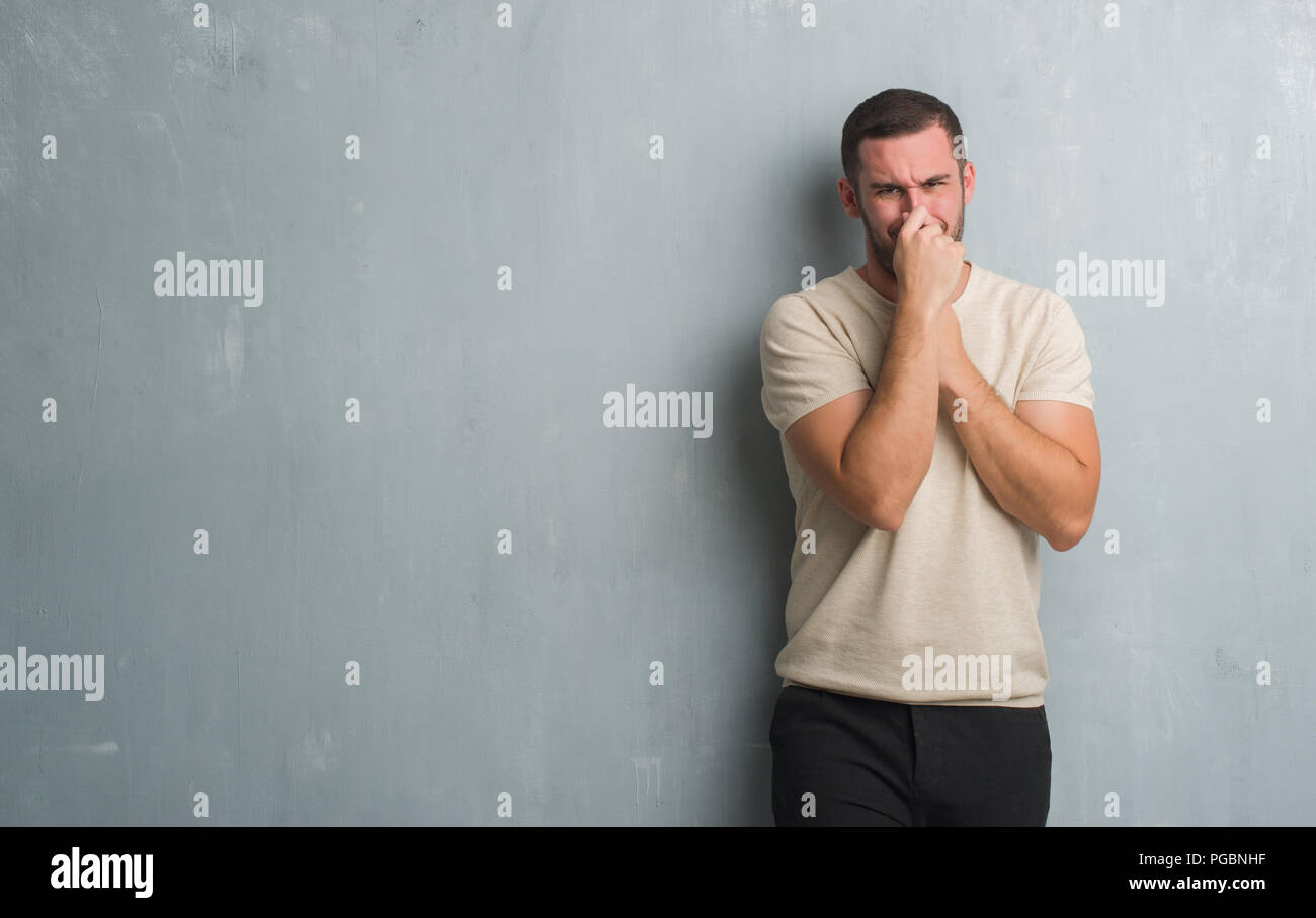 Young caucasian man over grey grunge wall smelling something stinky and ...