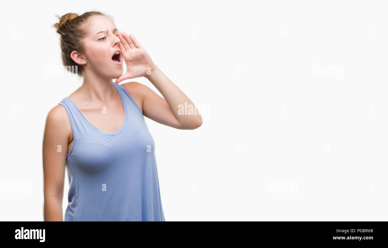 Young blonde woman shouting and screaming loud to side with hand on ...
