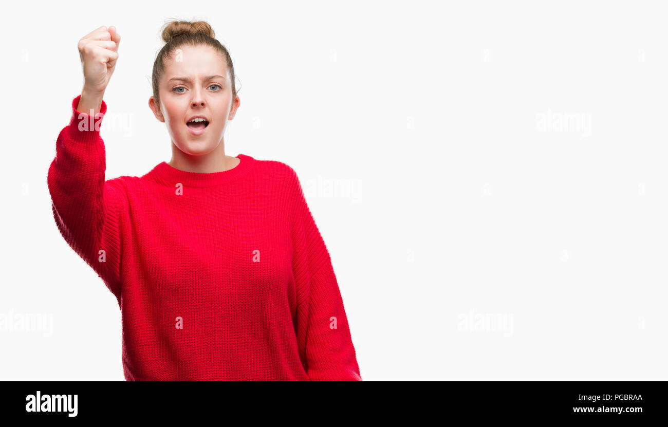 Young blonde woman wearing bun and red sweater angry and mad raising ...