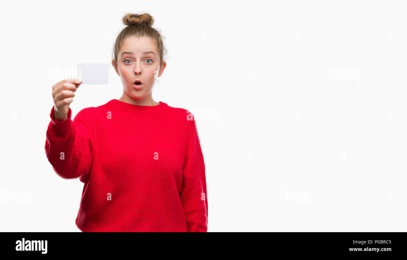 Young blonde woman holding advertising card scared in shock with a ...