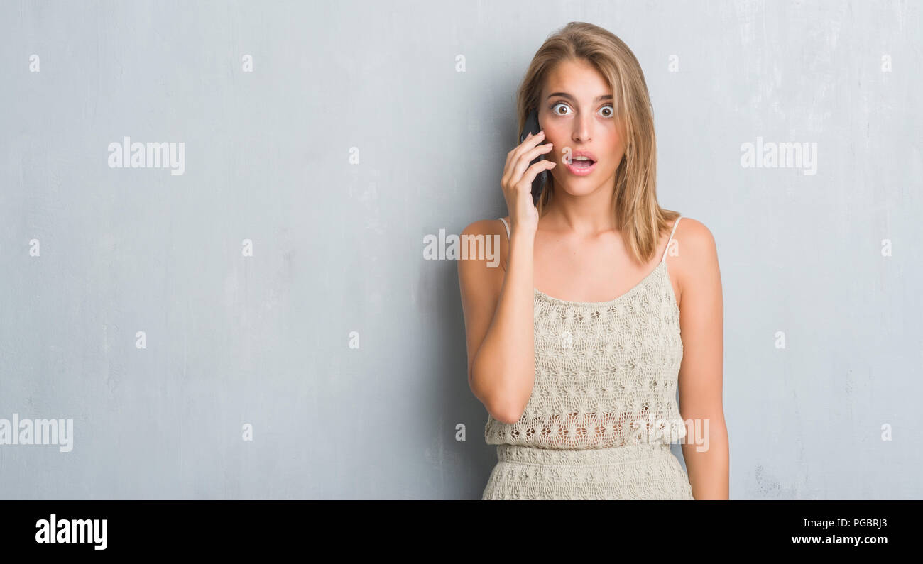 Beautiful young woman over grunge grey wall speaking on the phone ...