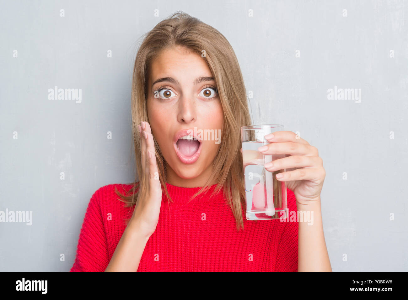 Beautiful young woman over grunge grey wall drinking a glass of water ...