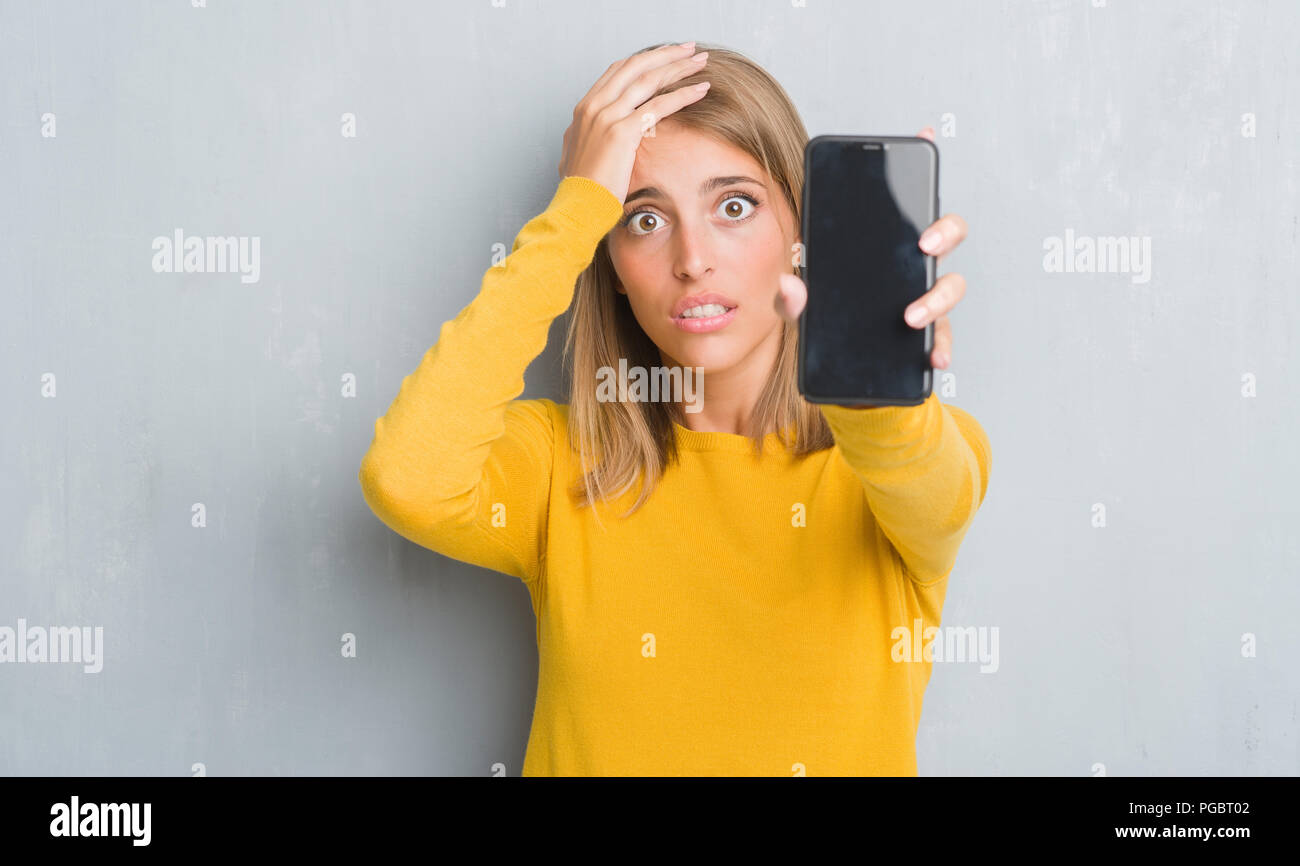 Beautiful young woman over grunge grey wall showing smartphone screen ...