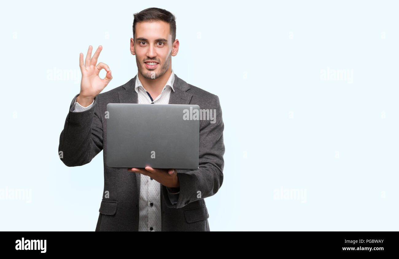 Handsome young man using computer laptop doing ok sign with fingers ...