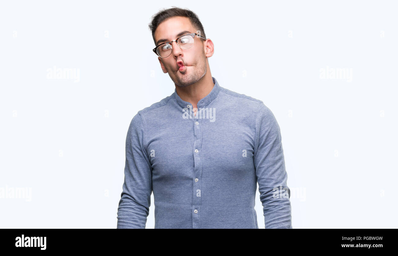 Handsome young elegant man wearing glasses making fish face with lips ...