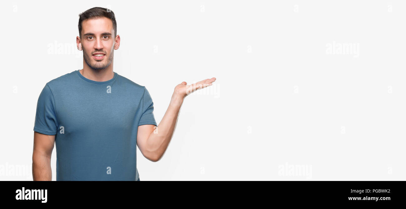 Handsome young casual man smiling cheerful presenting and pointing with ...
