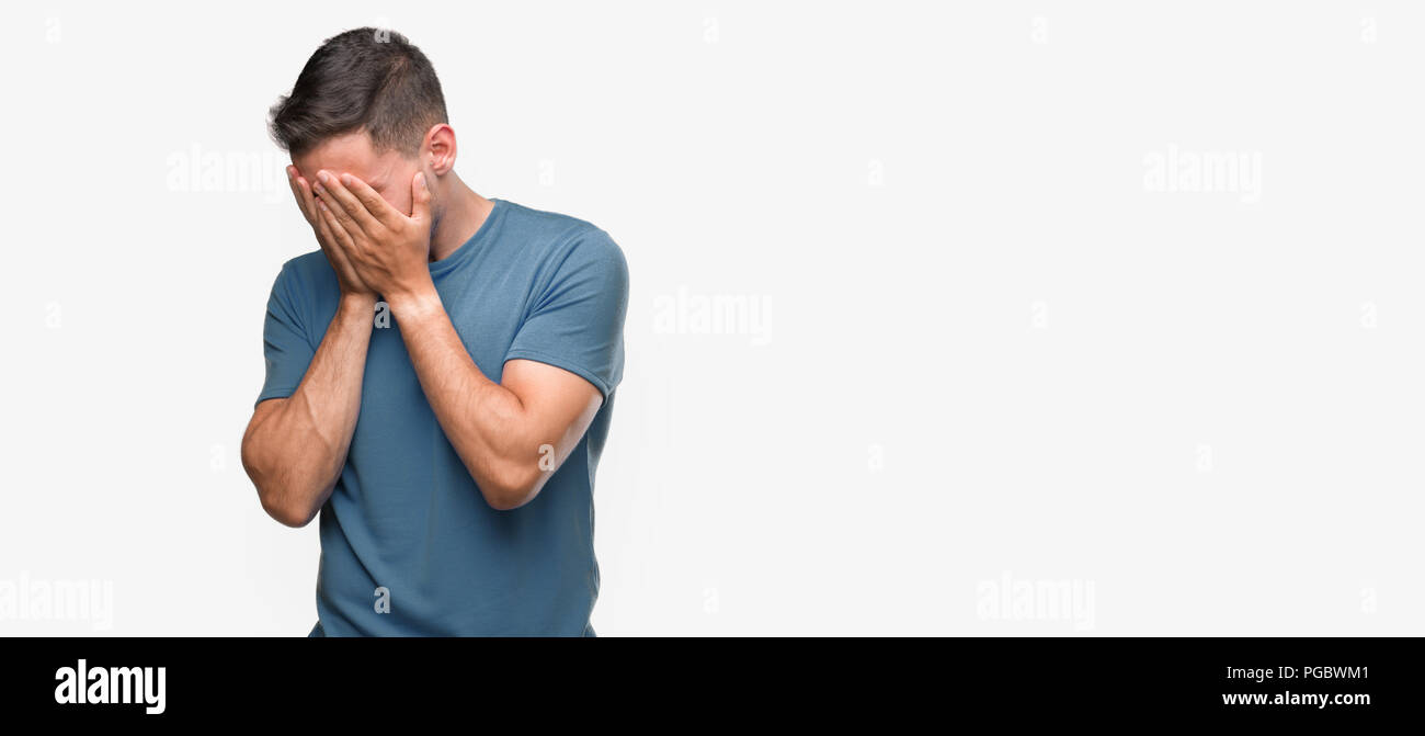 Handsome young casual man with sad expression covering face with hands ...