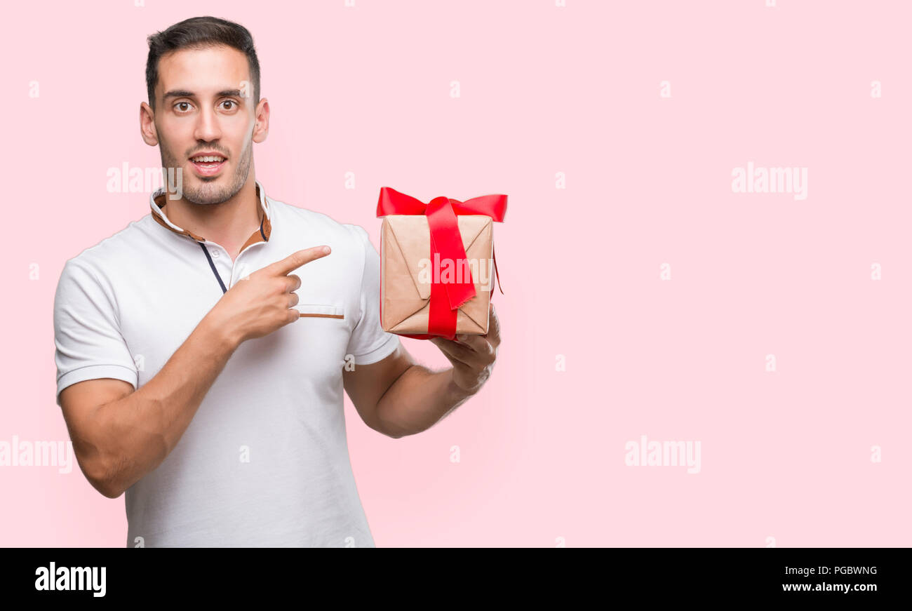 Handsome young man giving a present very happy pointing with hand and ...