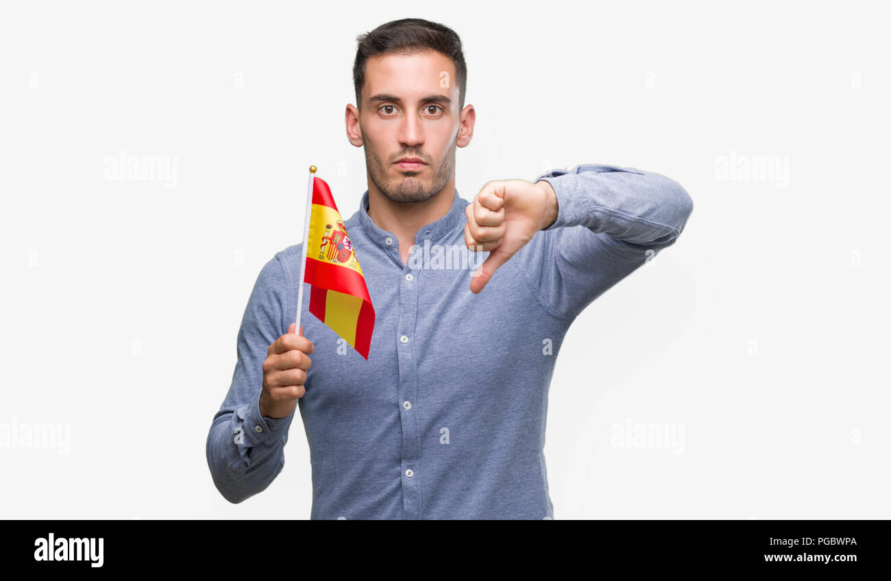 Handsome young man holding a flag of Spain with angry face, negative ...