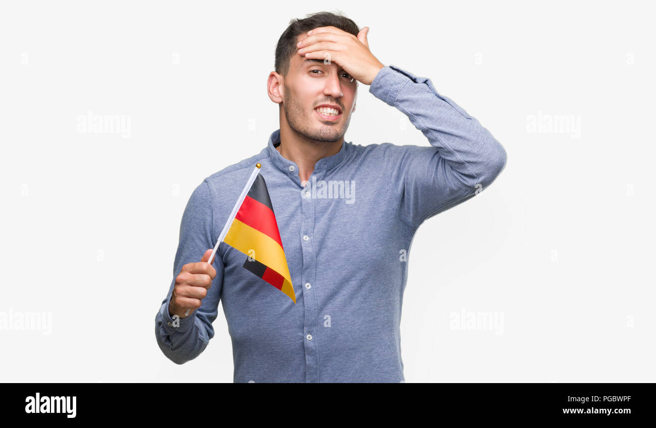 Handsome young man holding a flag of Germany stressed with hand on head ...