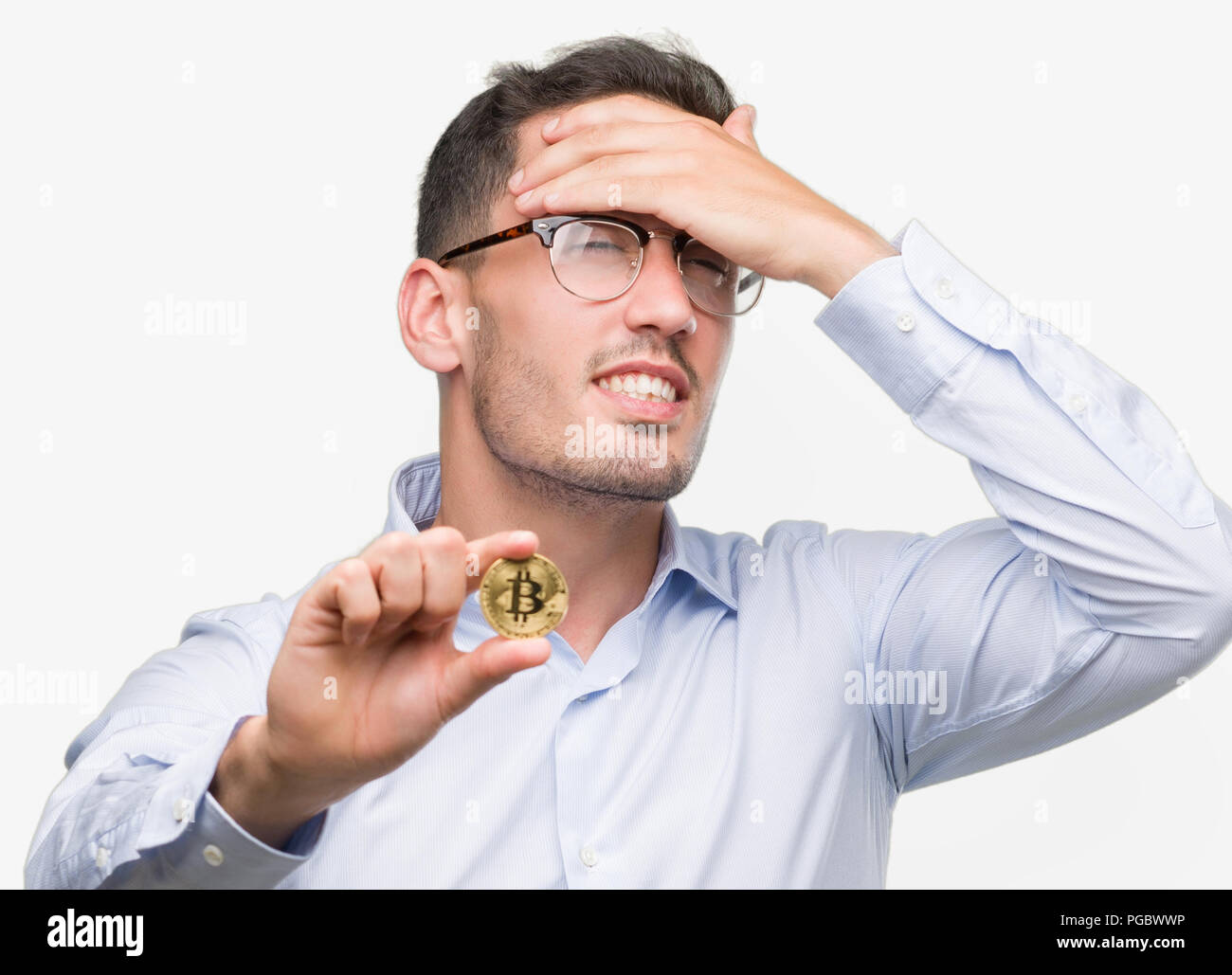 Handsome young man holding bitcoin stressed with hand on head, shocked ...