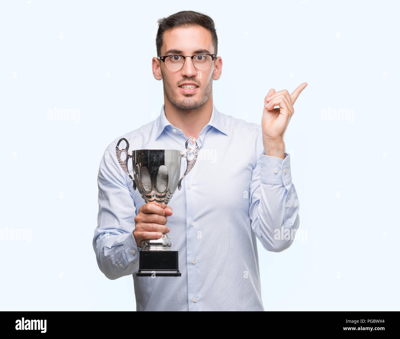 Handsome young man holding trophy very happy pointing with hand and ...