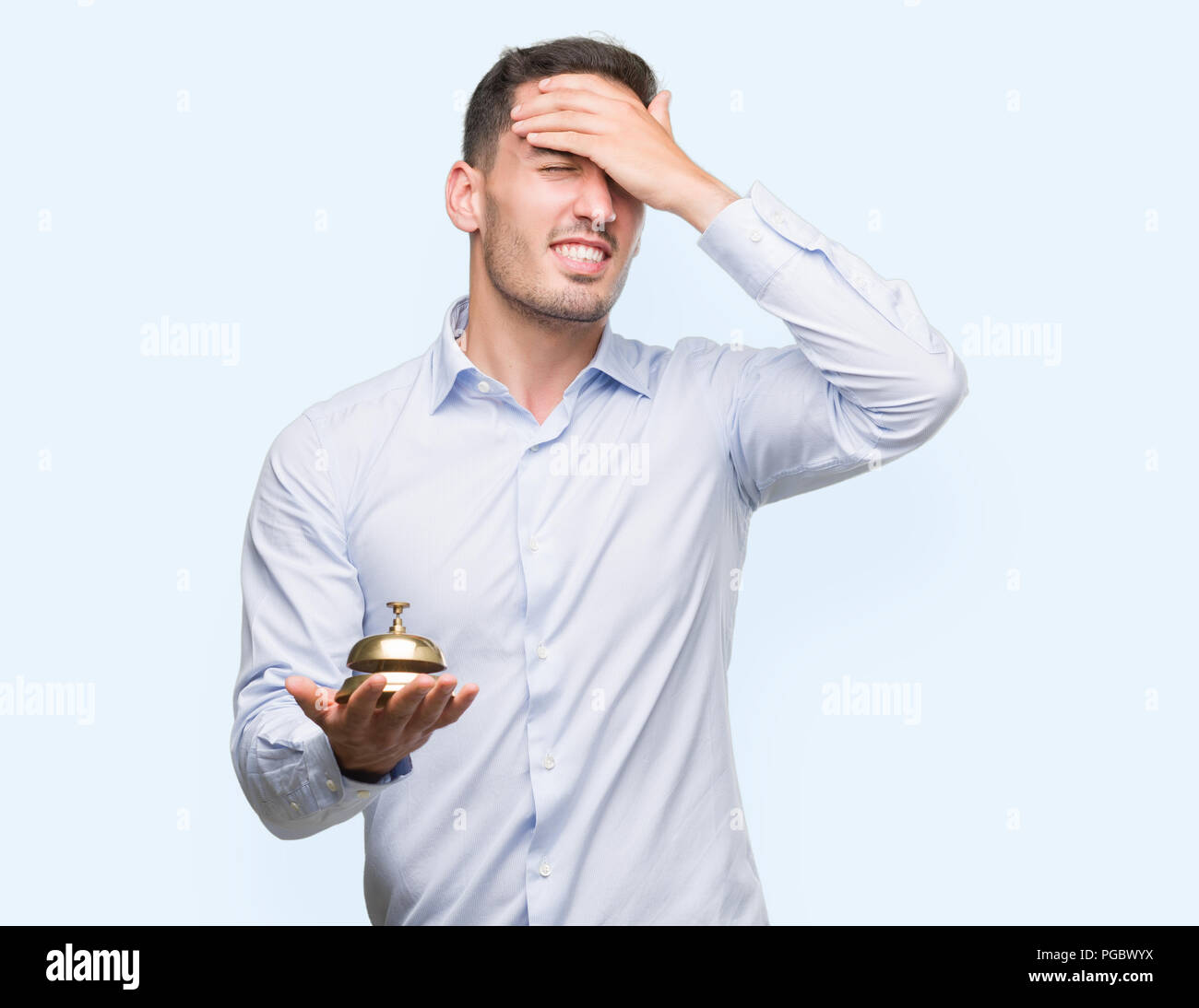 Handsome young man holding hotel ring bell stressed with hand on head ...