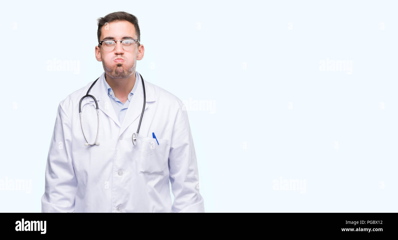 Handsome young doctor man puffing cheeks with funny face. Mouth ...