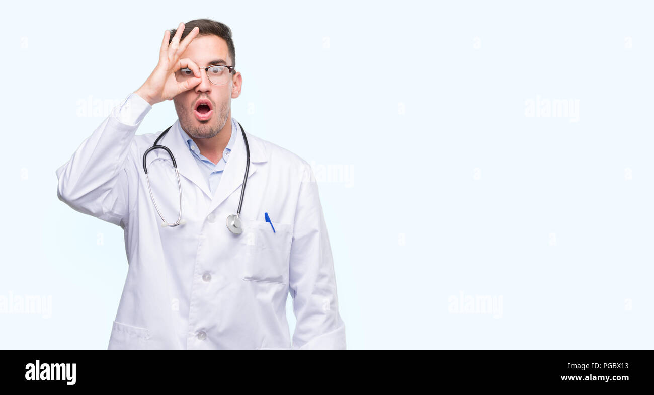 Handsome young doctor man doing ok gesture shocked with surprised face ...